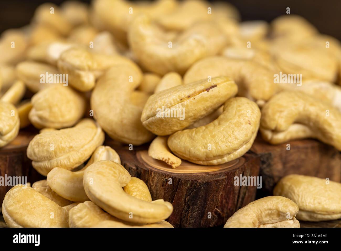 large cashew nuts are scattered on a larch board, raw unroasted cashew ...