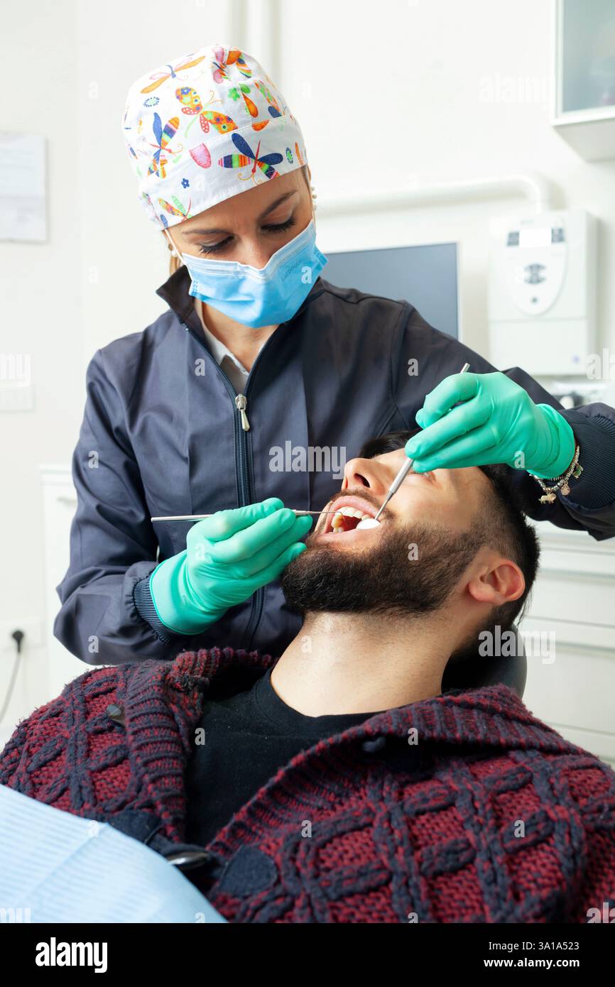 Female dentist examines a man patient in a dental office using ...
