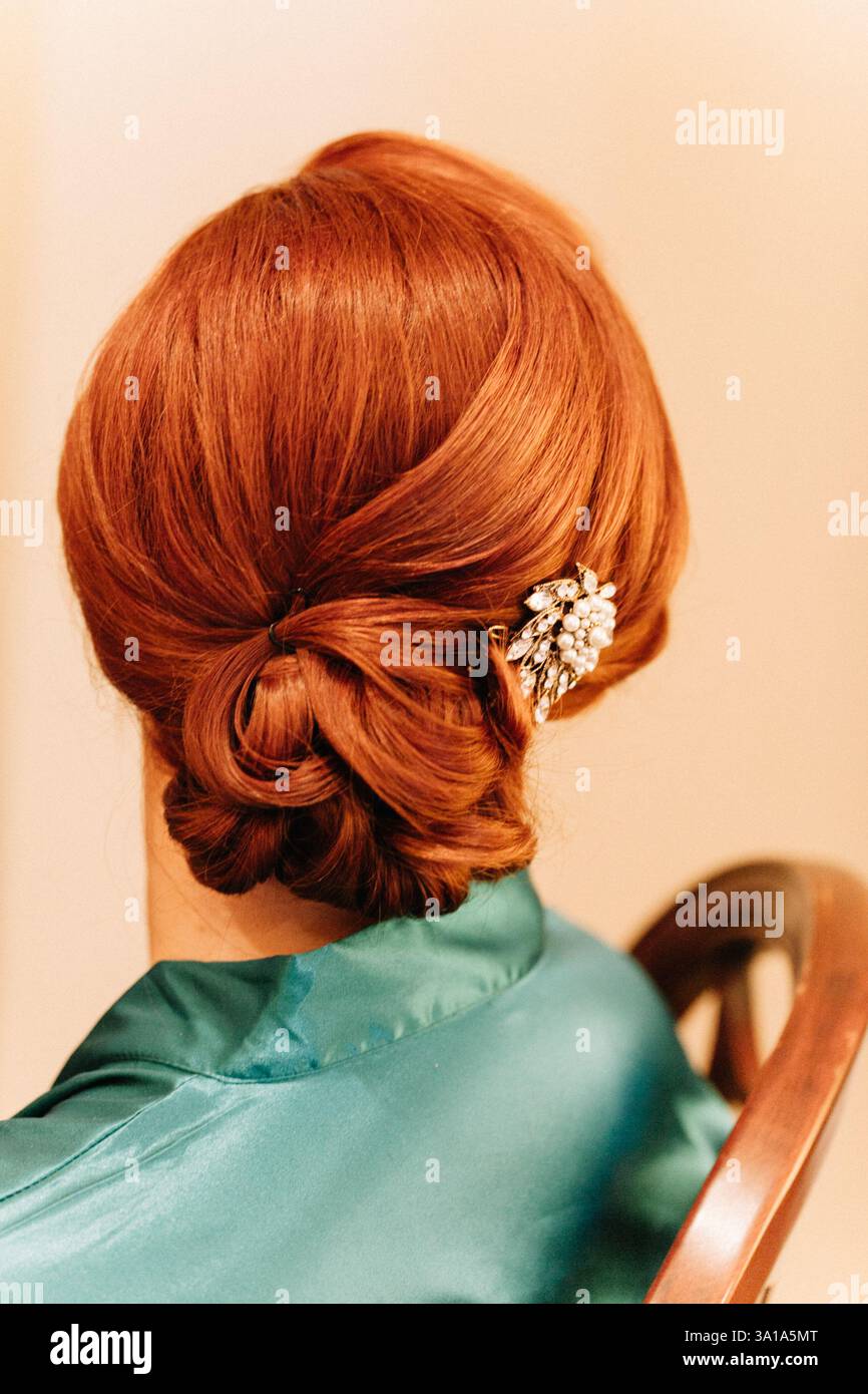 Rich red hair is styled in a polished updo with a decorative pin ...