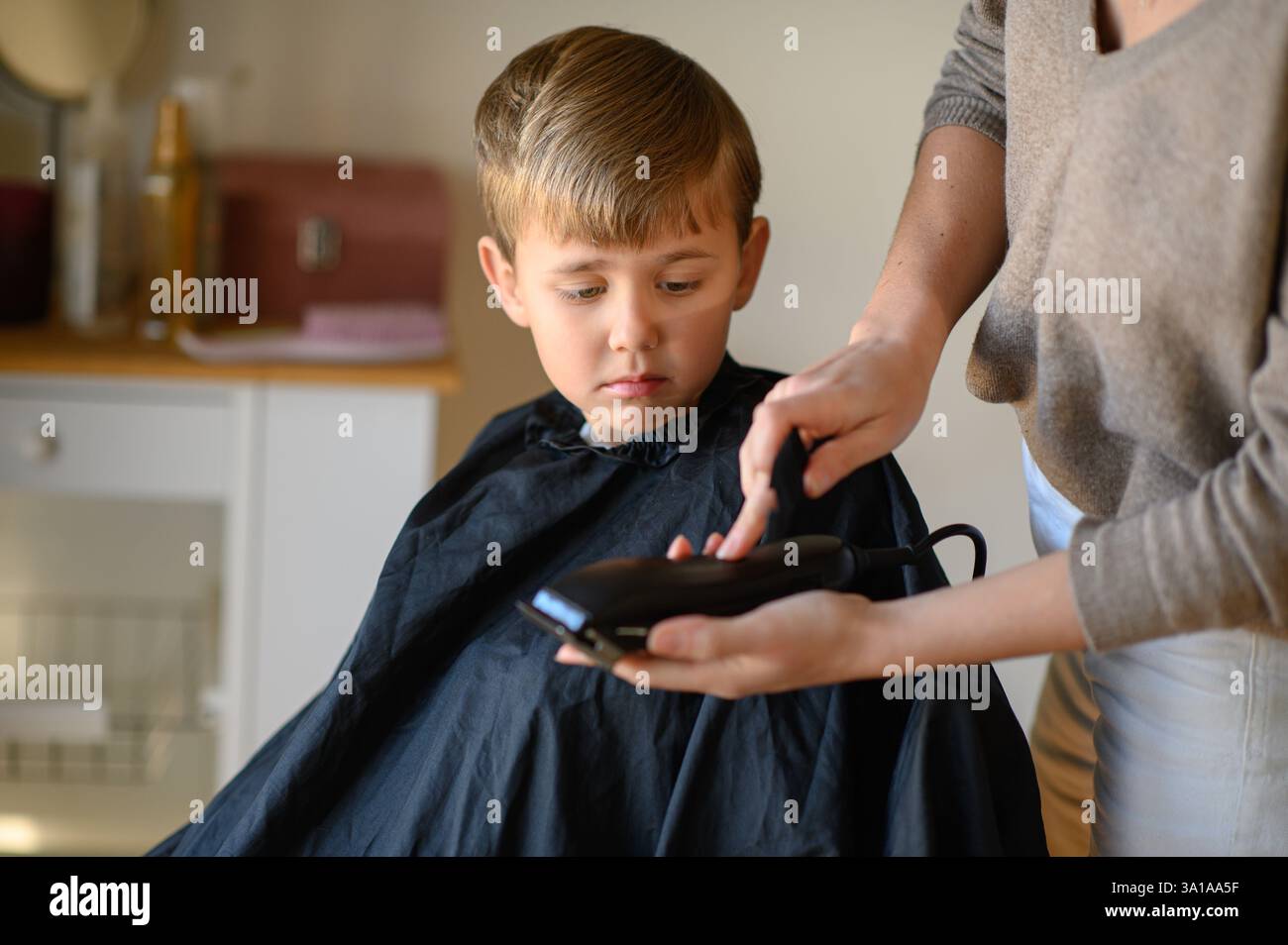 The hairdresser shows the boy the hair clipper and lets him touch it to ...