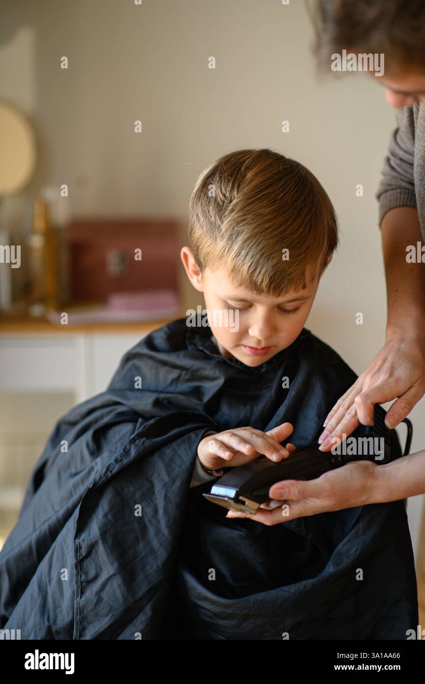 The hairdresser shows the boy the hair clipper and lets him touch it to ...