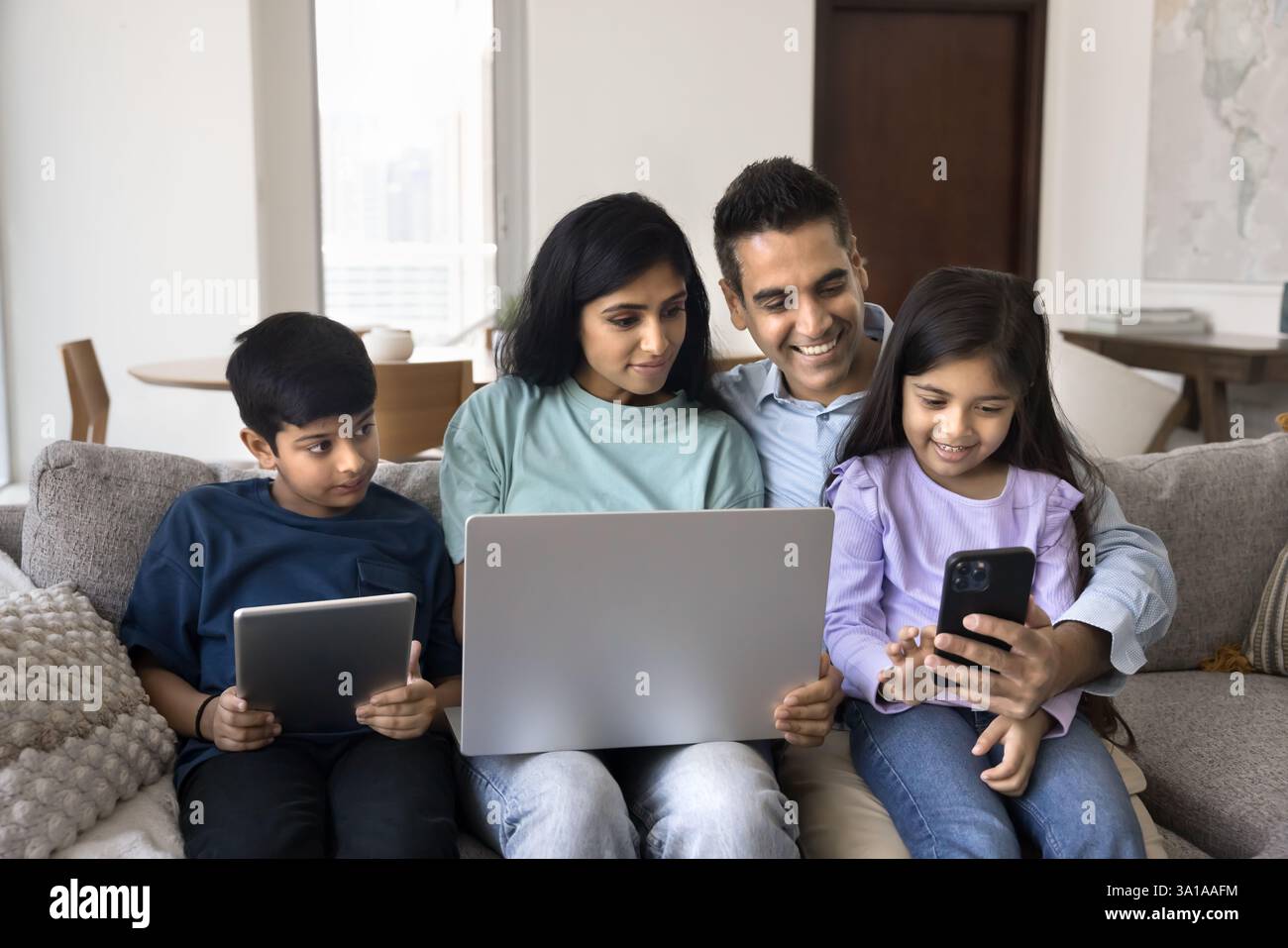 Indian family using diverse modern gadgets seated on couch Stock Photo ...