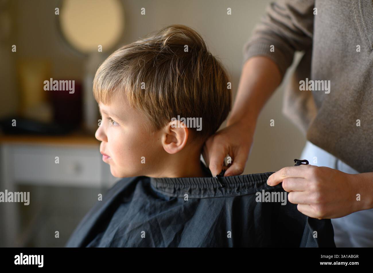 The hairdresser is putting a protective cape on the boy for a haircut ...