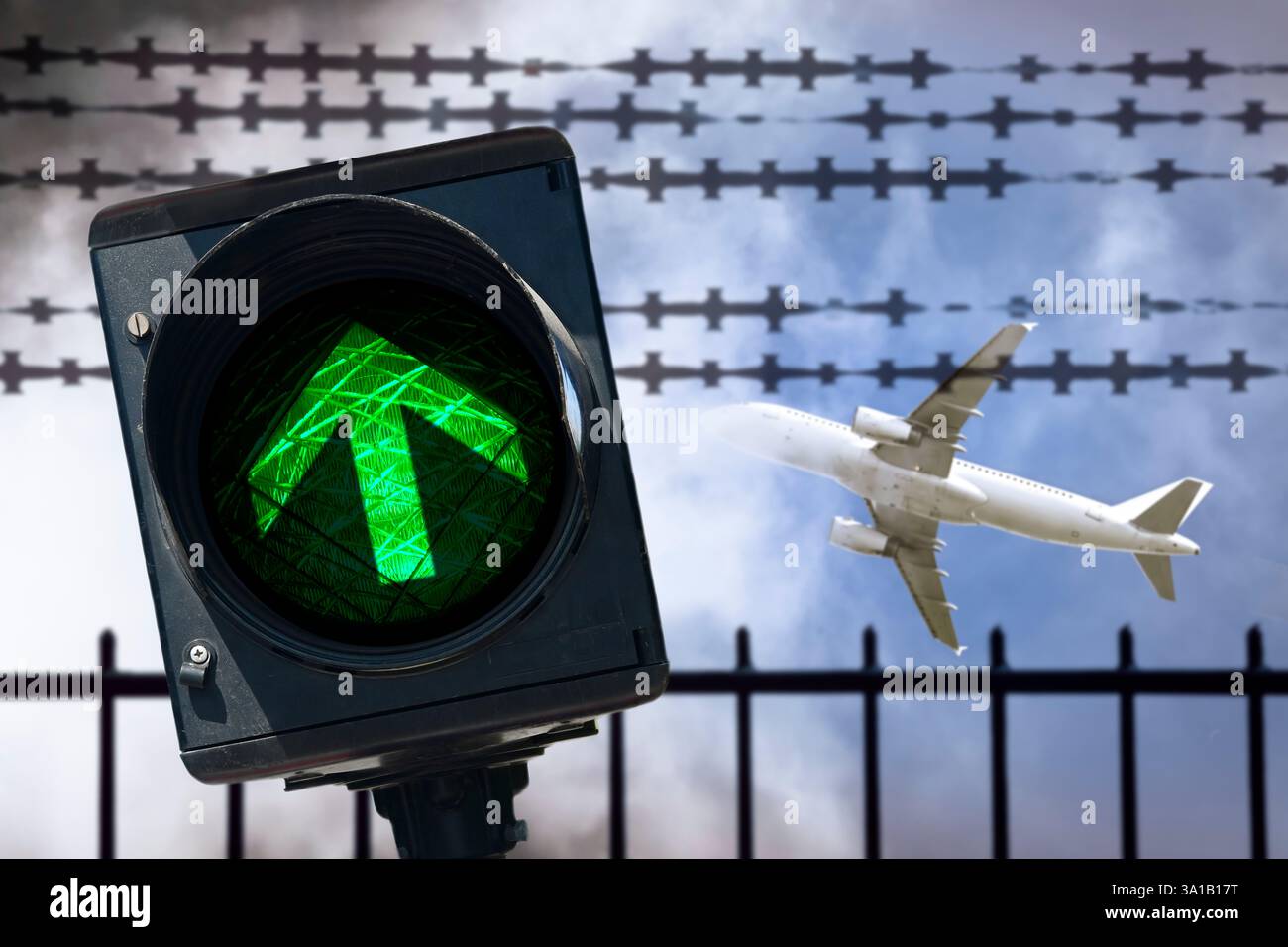 Barbed wire and green traffic light in front of a plane taking off ...