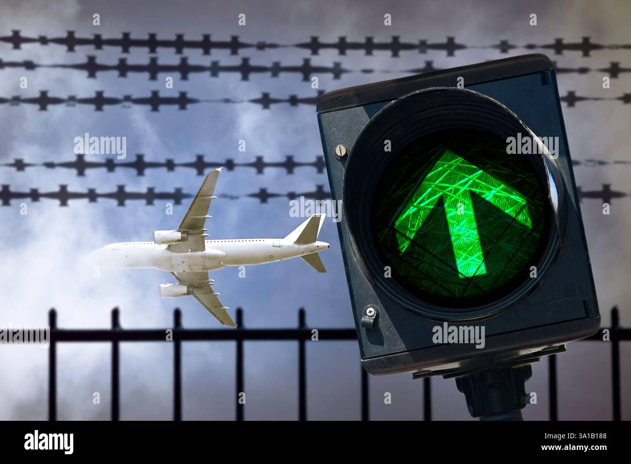 Barbed wire and green traffic light in front of a plane taking off ...