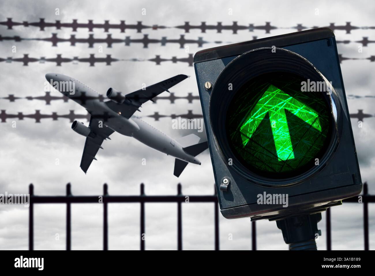 Barbed wire and green traffic light in front of a plane taking off ...