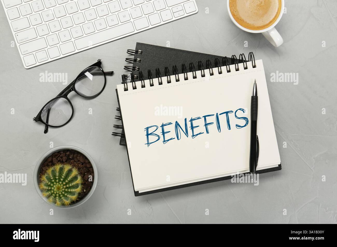 Benefits word in notebook, pen, coffee, eyeglasses and computer keyboard on grey table, top view ...
