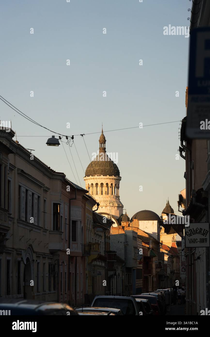 Sunset view of Church in Cluj, Romania. Buildings line a narrow street ...