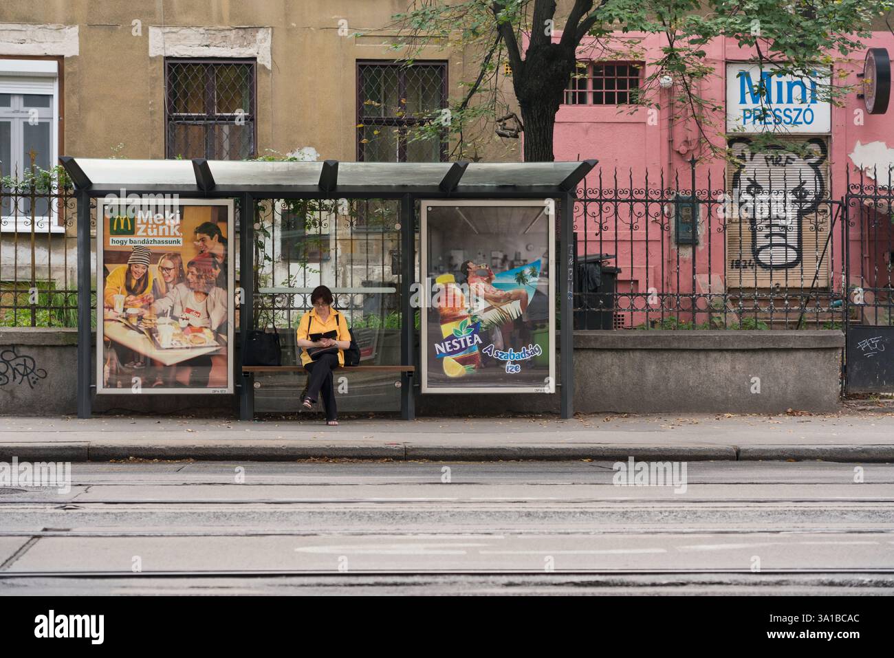 Woman sits on a bus stop bench in Budapest, Hungary, near a tram track ...