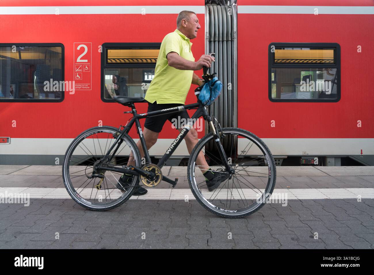 Man walks a bike along a train platform at a German train station ...