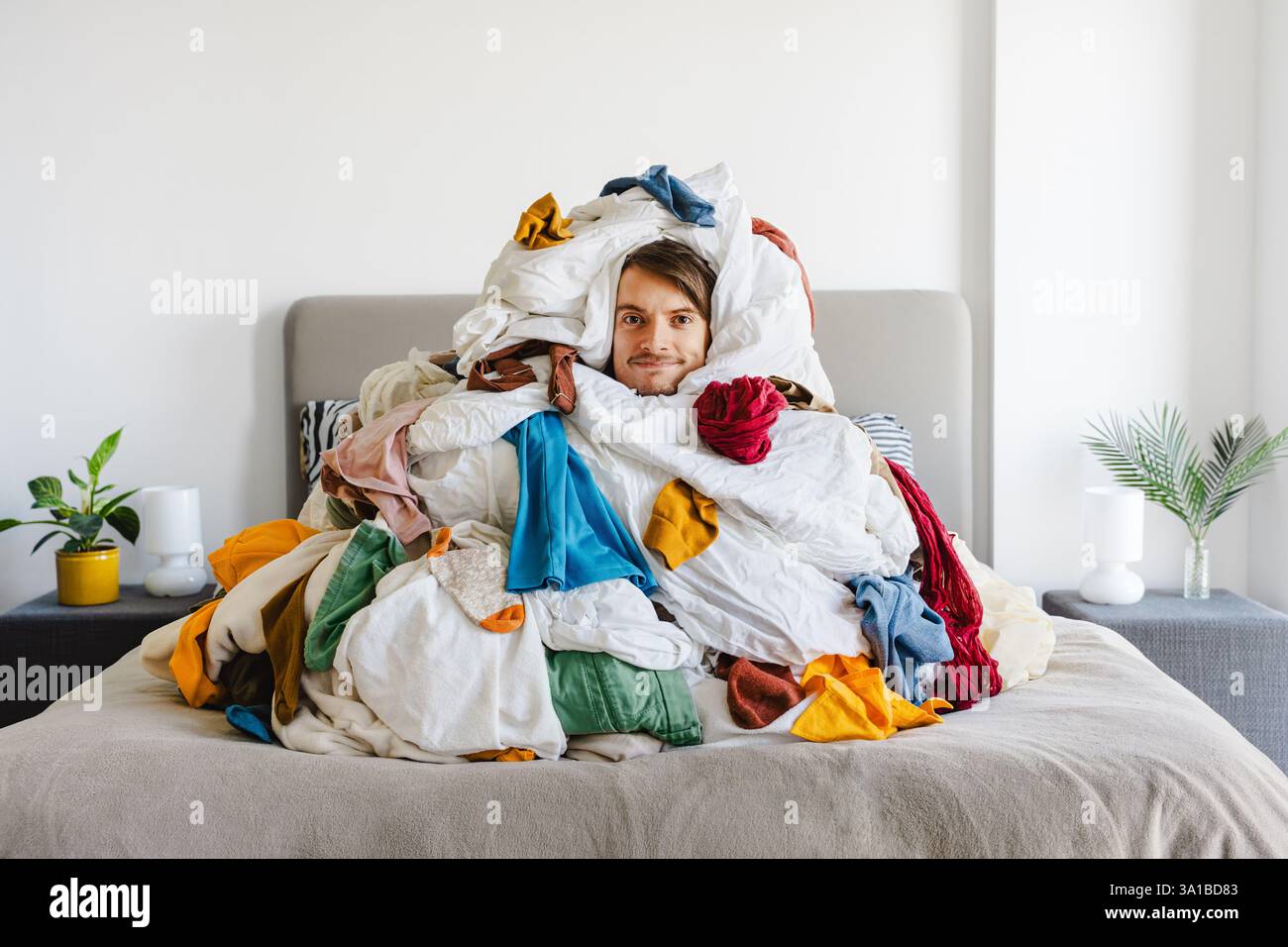 A man head peeks out from a massive pile of mixed laundry on a bed ...