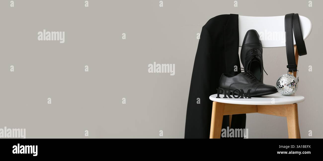 Word PROM, shoes, suit and disco ball on chair against grey background ...