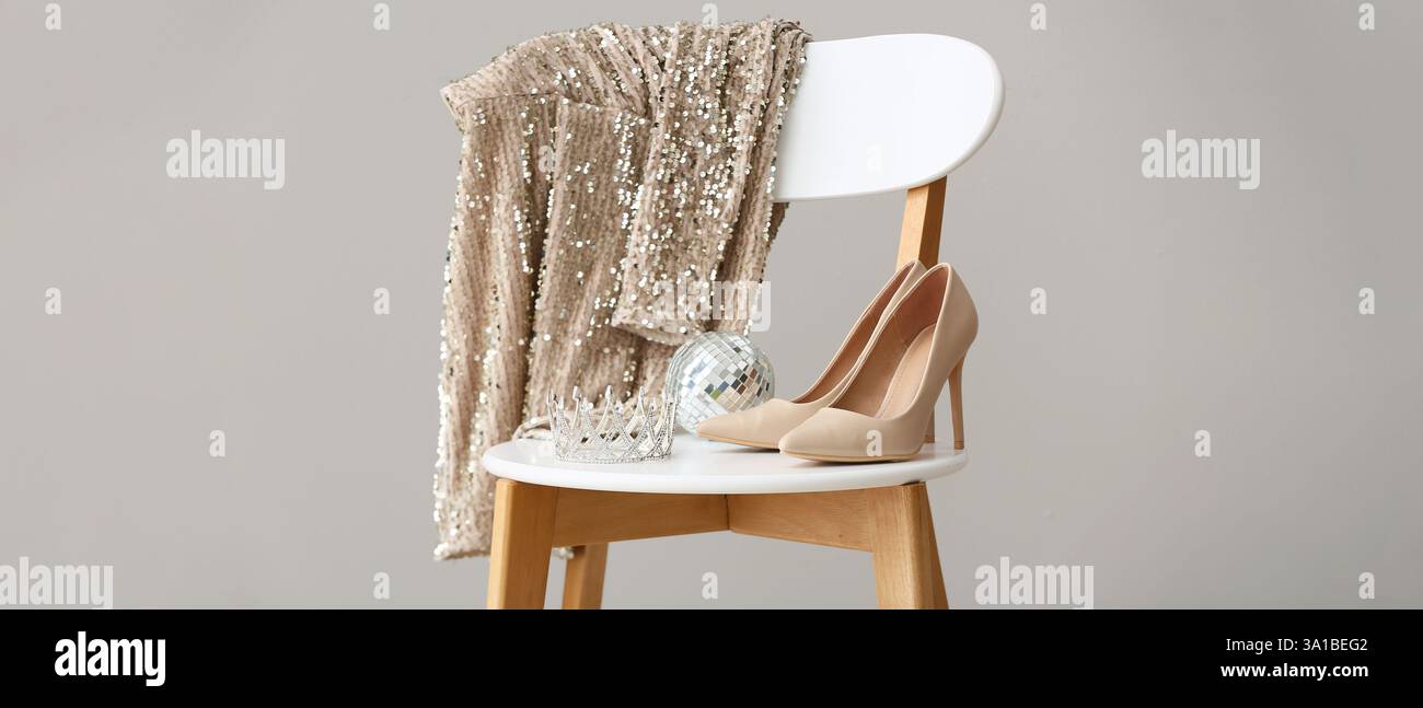 Prom dress, shoes, crown and disco ball on chair against grey ...