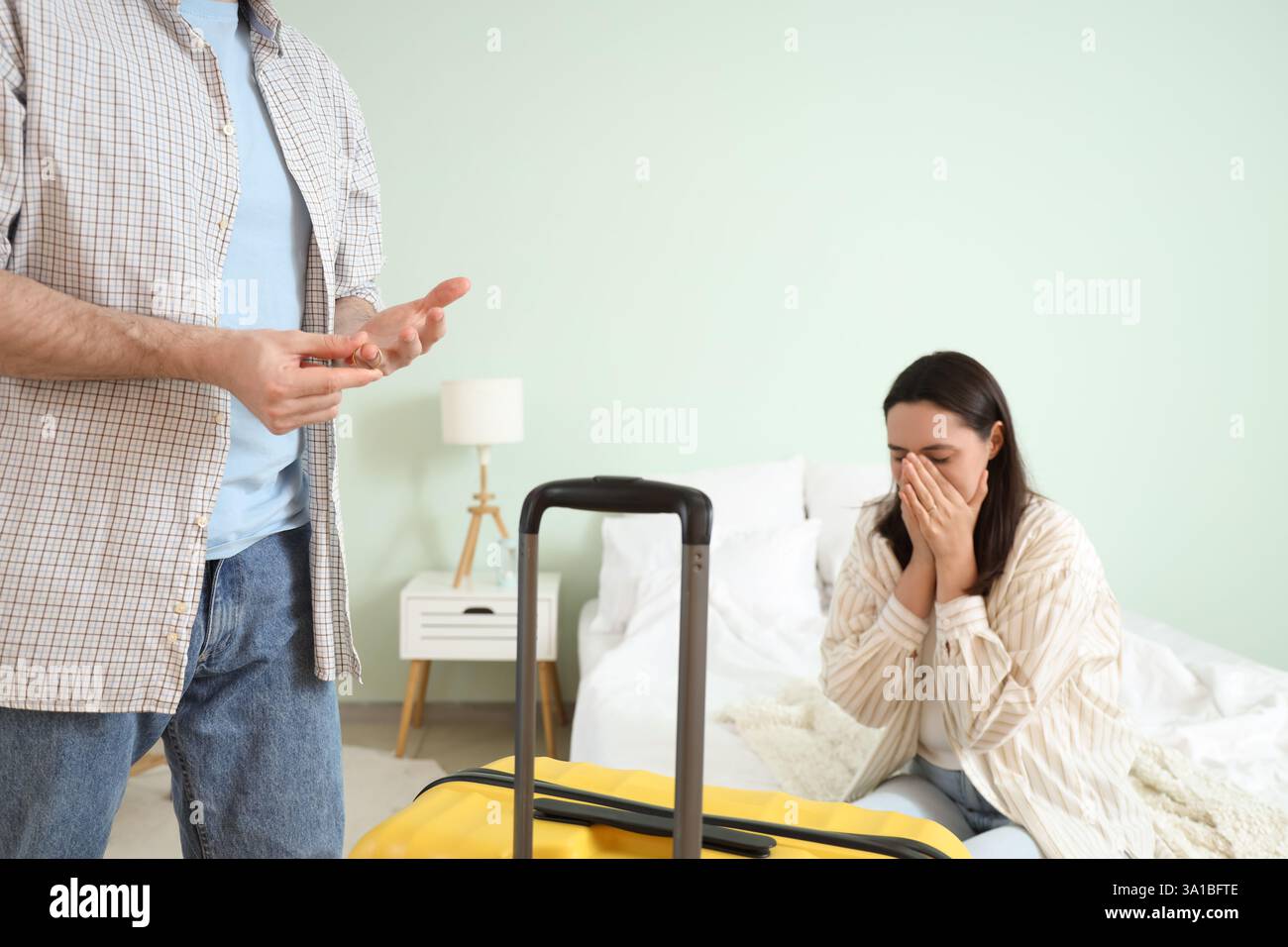 Young man taking wedding ring off finger with suitcase and crying wife ...