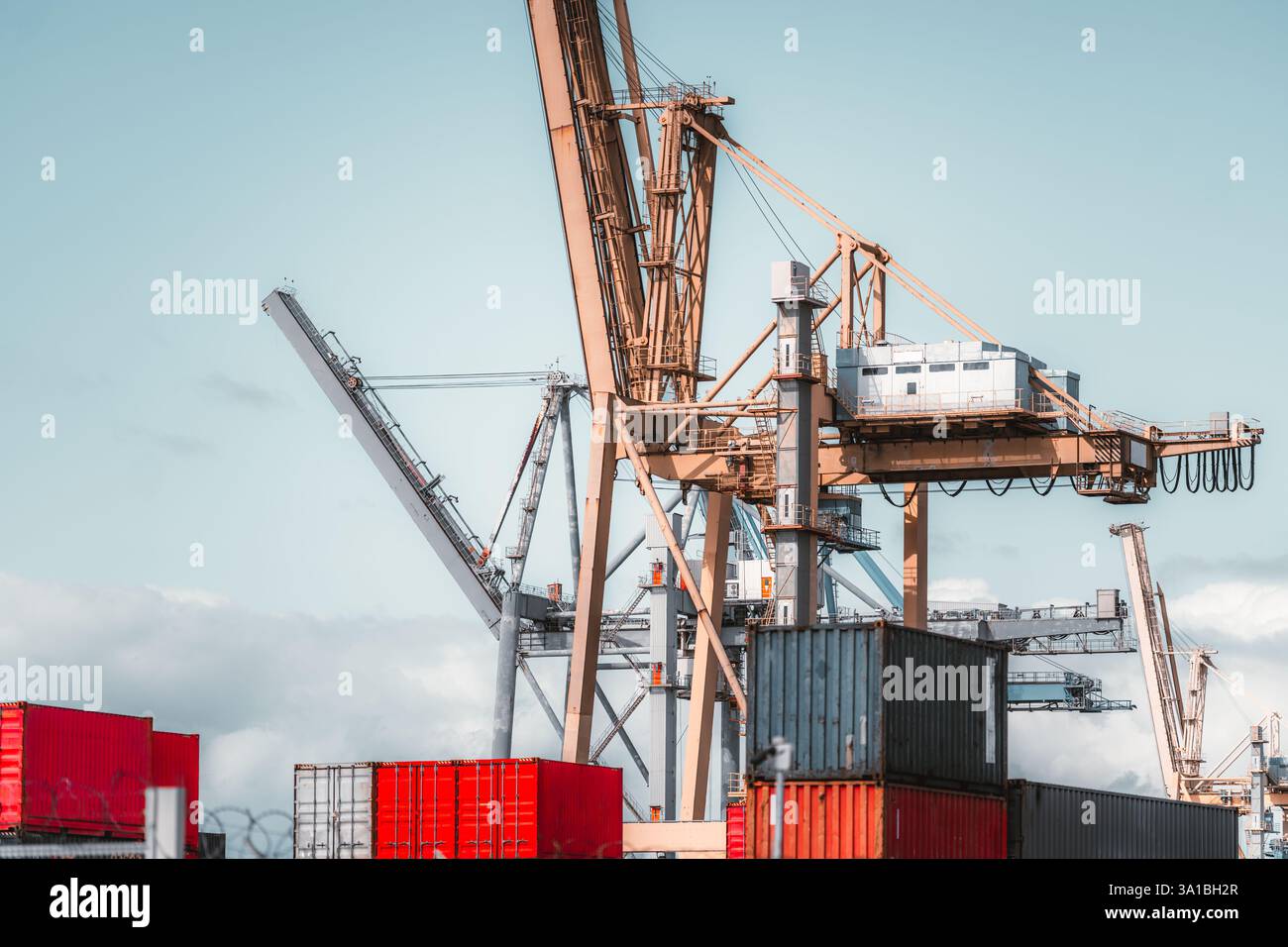 A telephoto view of a large industrial shipping port with towering container cranes unloading ...