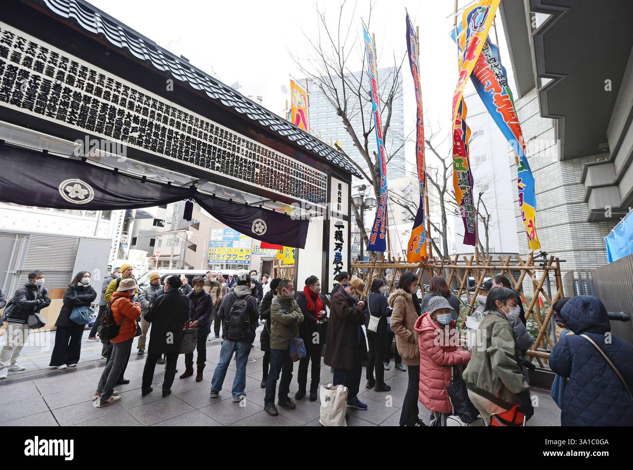 Sumo fans line up in front of a row flags bearing the name of a sumo ...