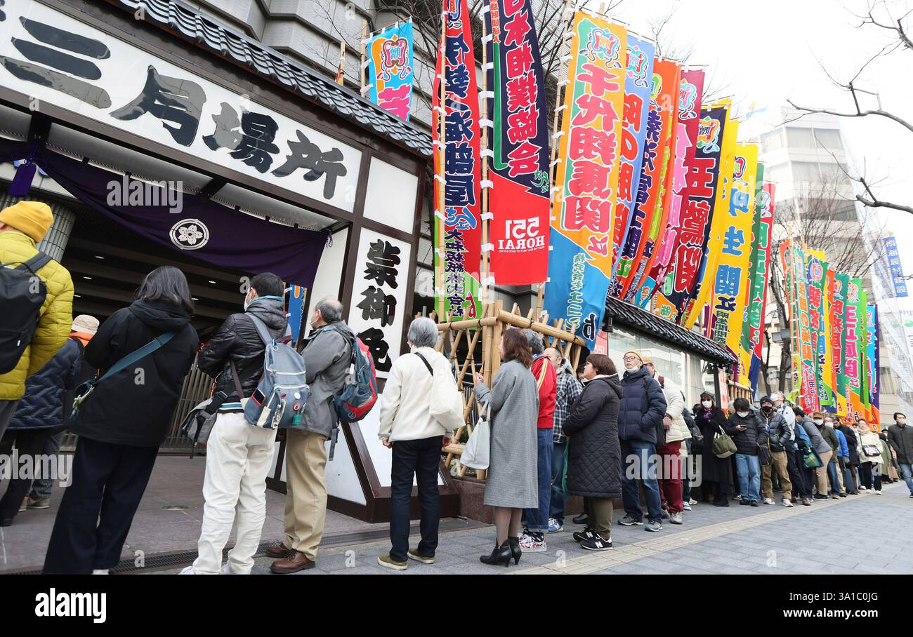 Sumo fans line up in front of a row flags bearing the name of a sumo ...