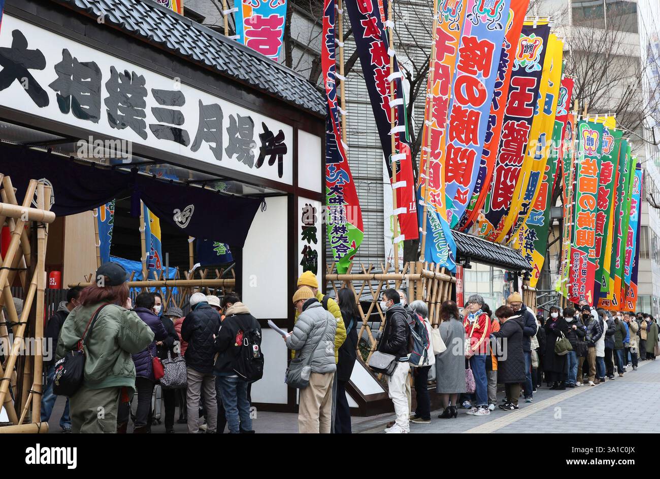 Sumo fans line up in front of a row flags bearing the name of a sumo ...