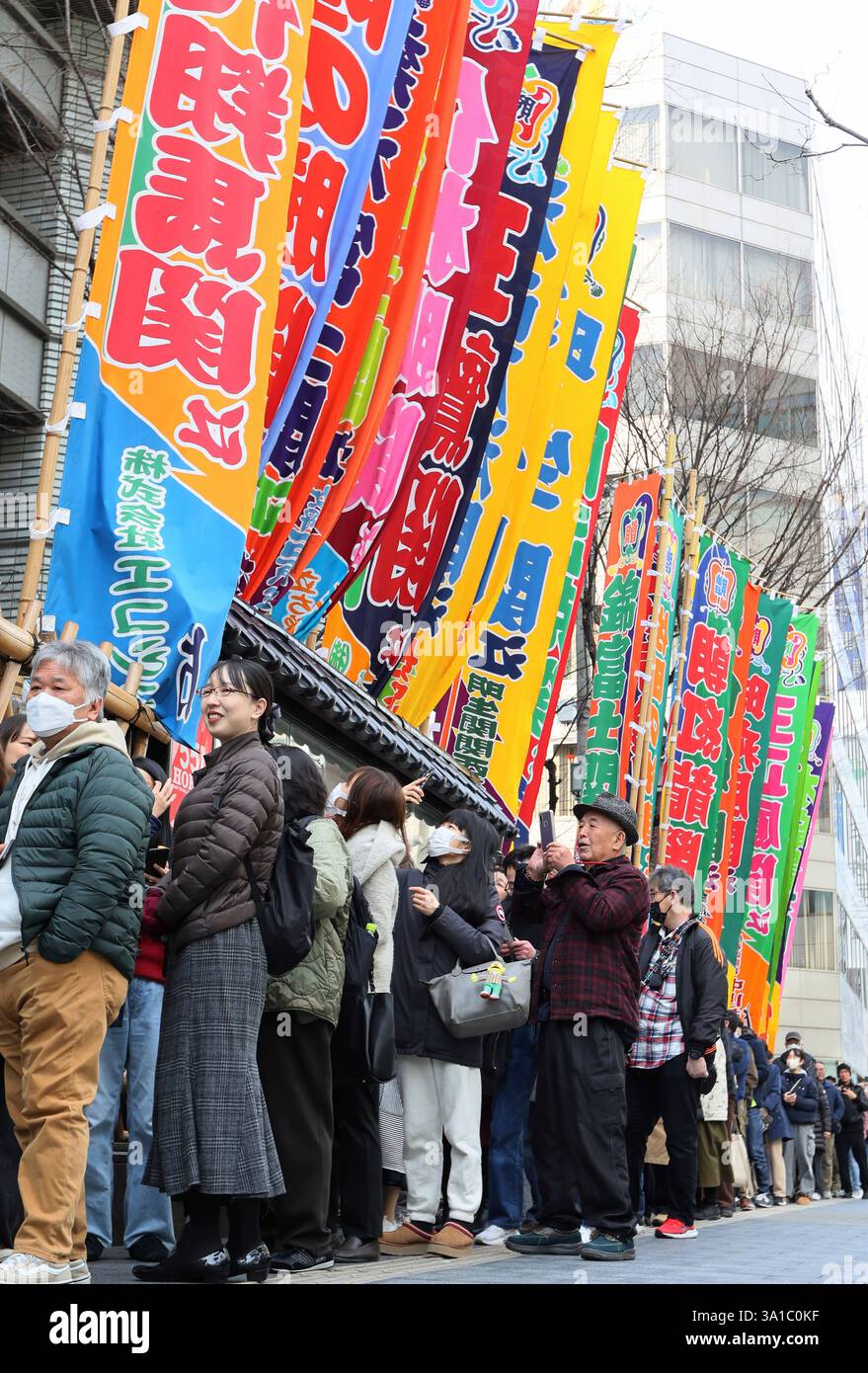Sumo fans line up in front of a row flags bearing the name of a sumo ...