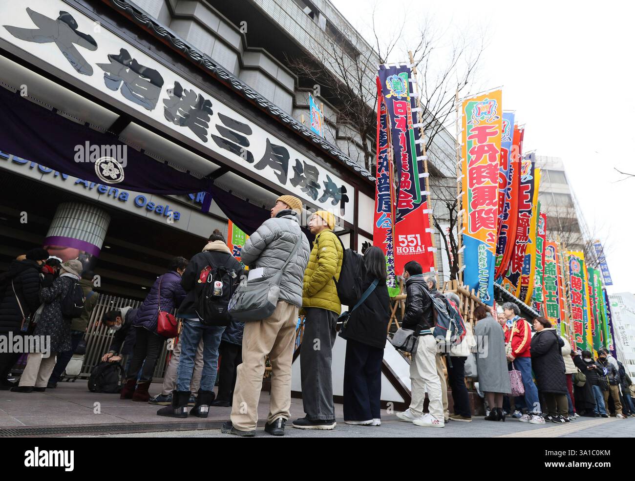 Sumo fans line up in front of a row flags bearing the name of a sumo ...