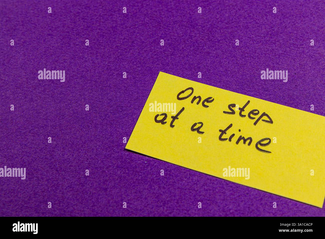A yellow sticky note with the text One step at a time rests on a purple ...