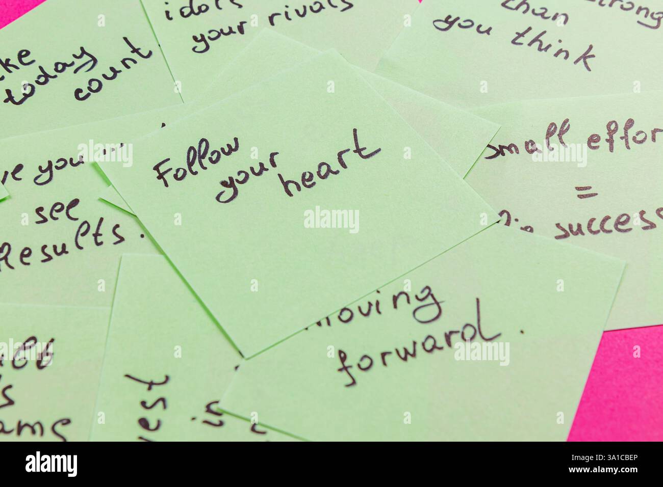 A collection of handwritten motivational notes lies on a bright pink ...