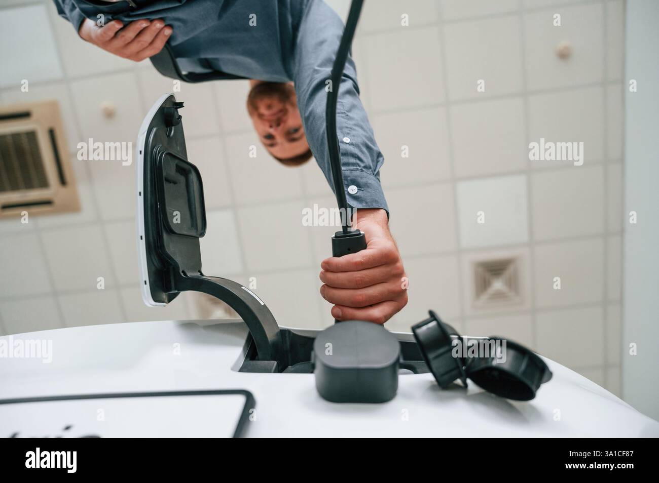 View from below. Plugging the charger. Handsome car dealership worker ...