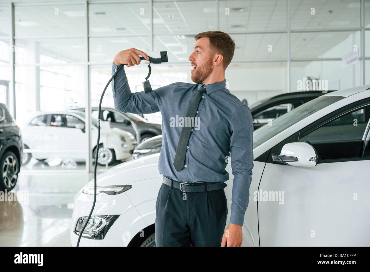 Smiling, holding the charger. Handsome car dealership worker is with ...