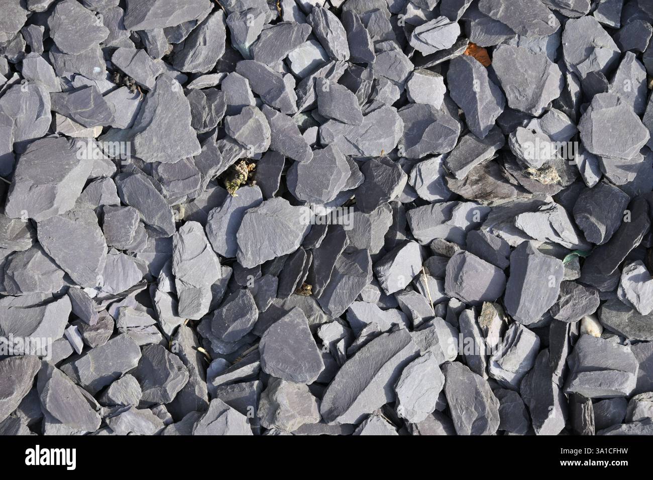 A pile of gray rocks with some green grass growing in between. The ...