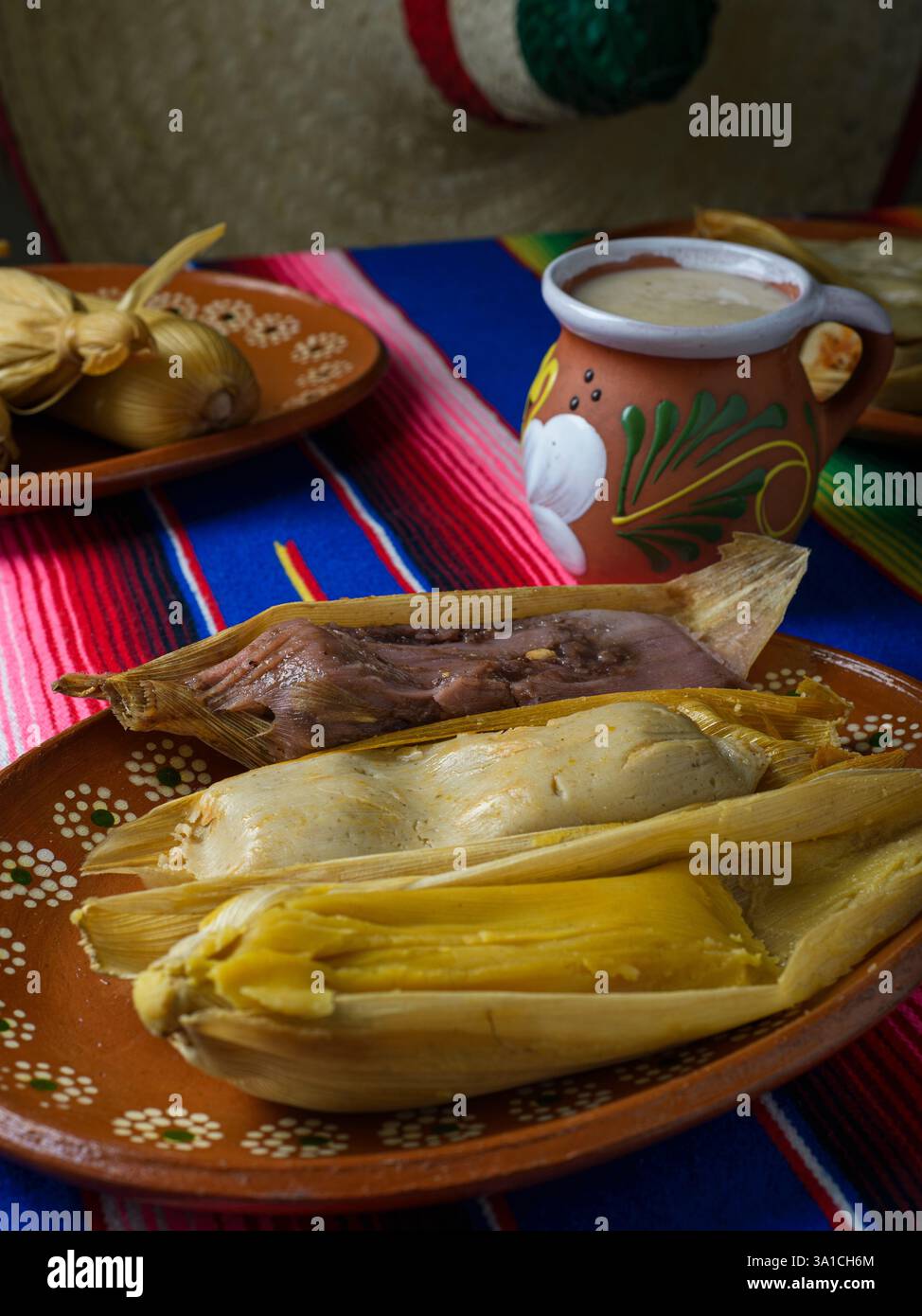 Tamales of different flavors in a clay dish and cup of atole on a ...