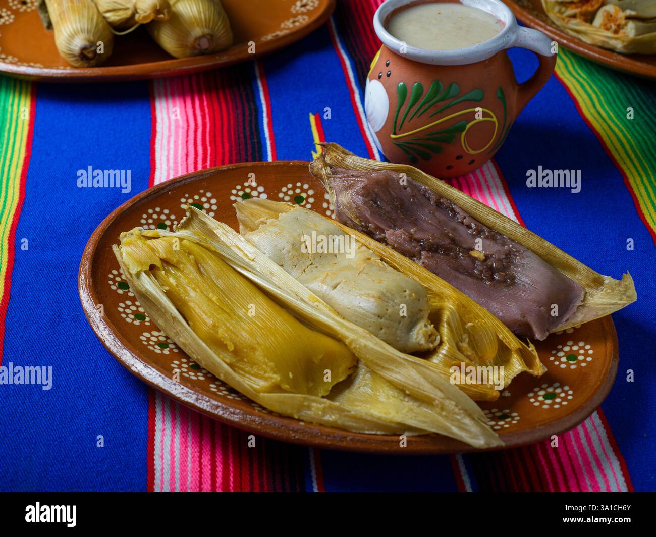 Tamales of different flavors in a clay dish and cup of atole on a ...