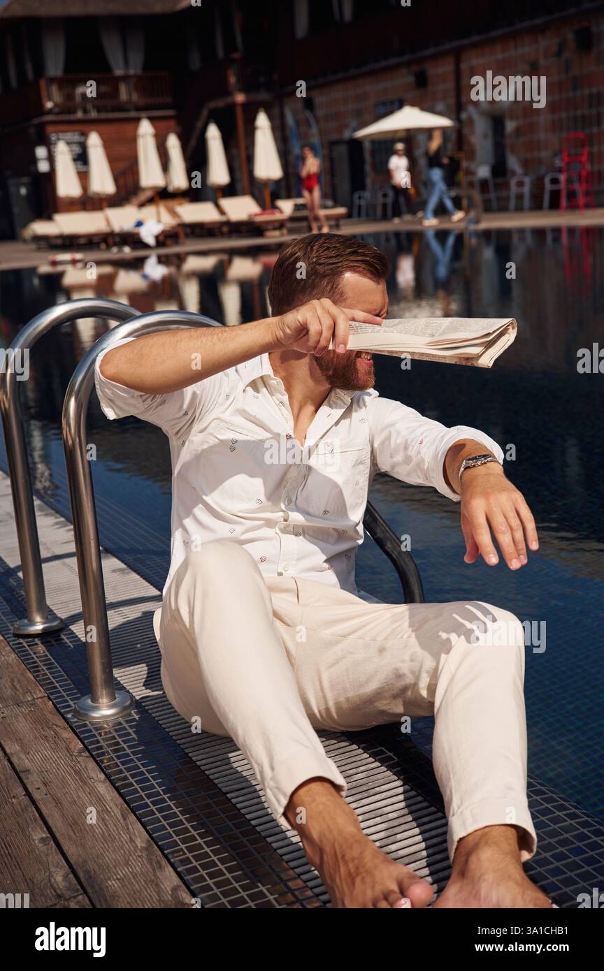 Covering himself by newspaper from bright sunlight. Handsome man in ...
