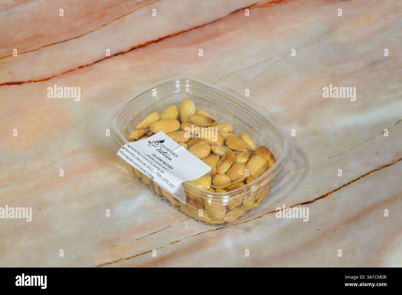 A plastic container of nuts sits on a marble countertop. The nuts are ...