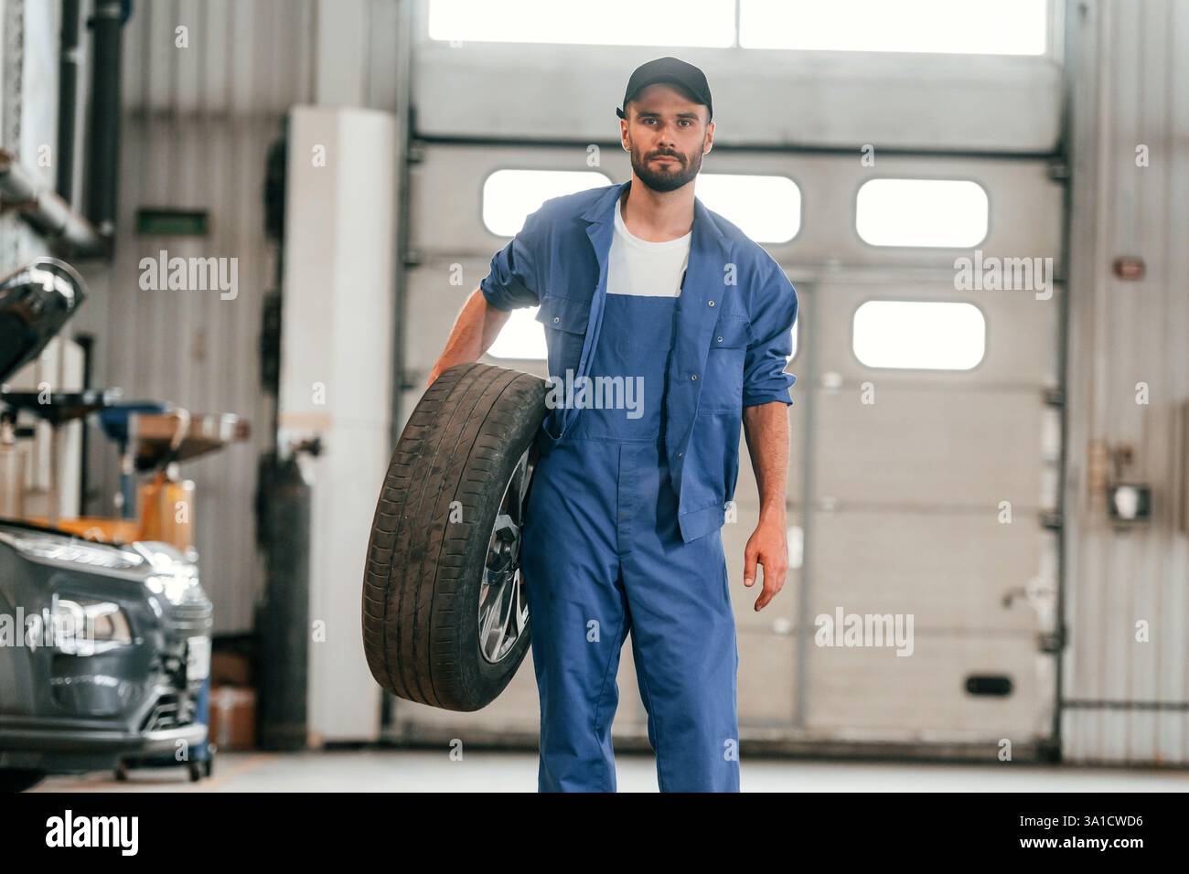 Front view, standing and holding tire. Auto mechanic working in garage ...