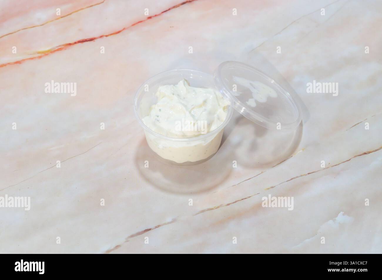 A small plastic container filled with white cream is placed on a marble ...