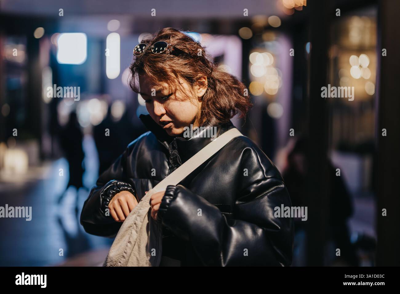 Person exploring through a bag on a bustling city street at night Stock ...