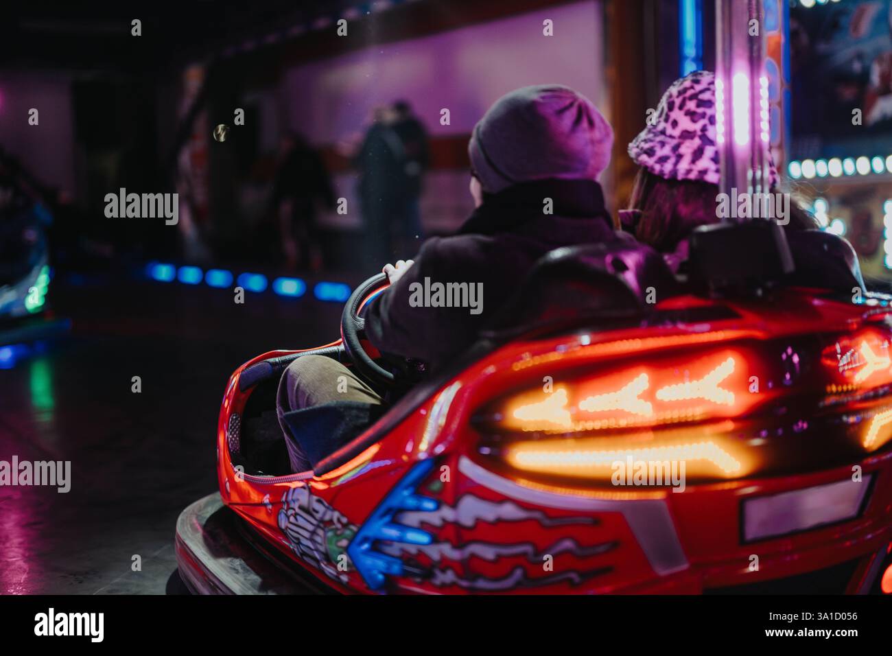 Couple enjoying a ride on a brightly lit bumper car at an indoor fair ...