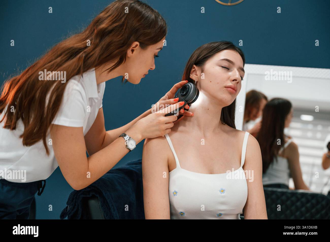 Beauty salon worker is examining skin of the woman by using a device ...