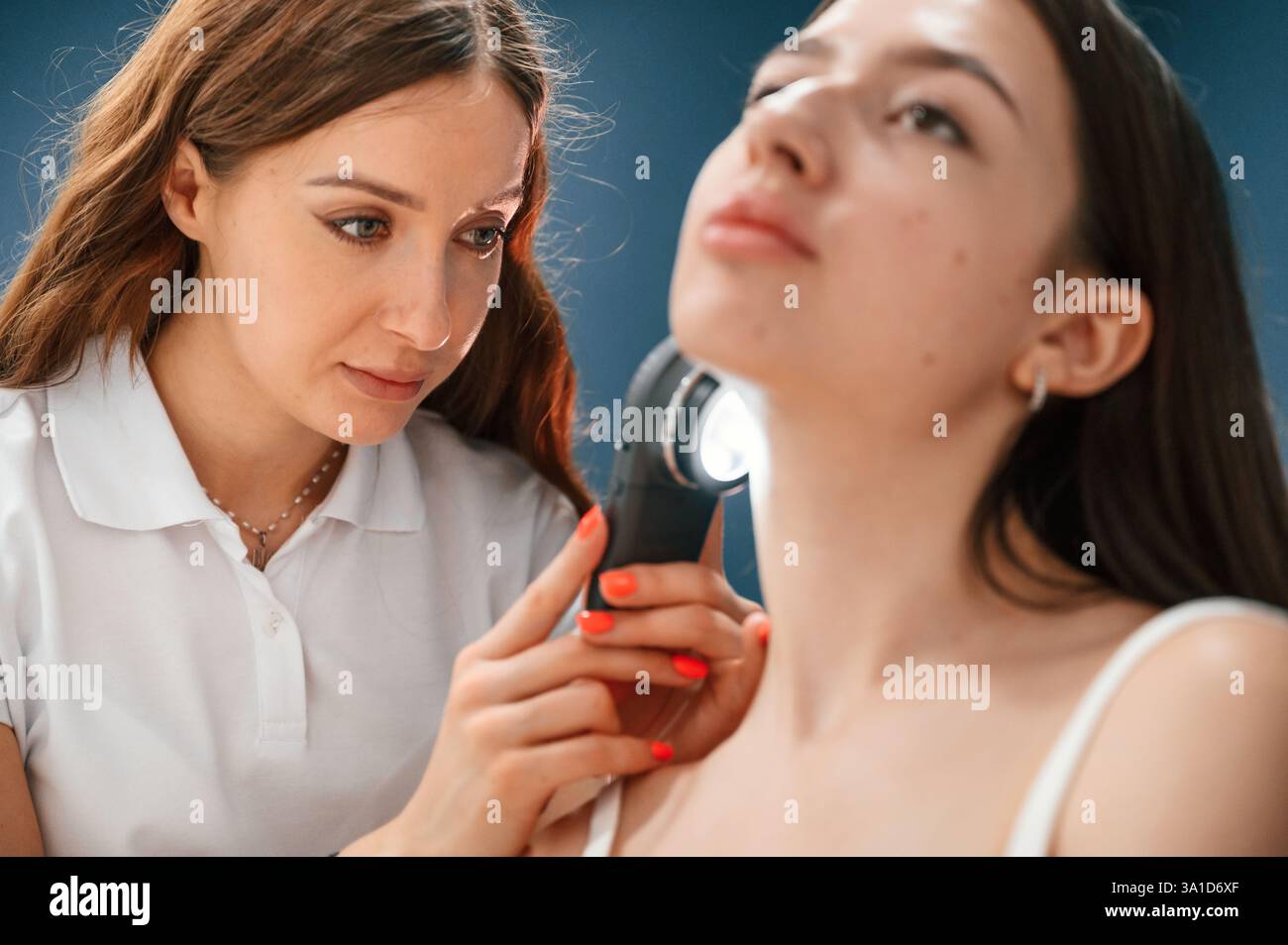 Beauty salon worker is examining skin of the woman by using a device ...