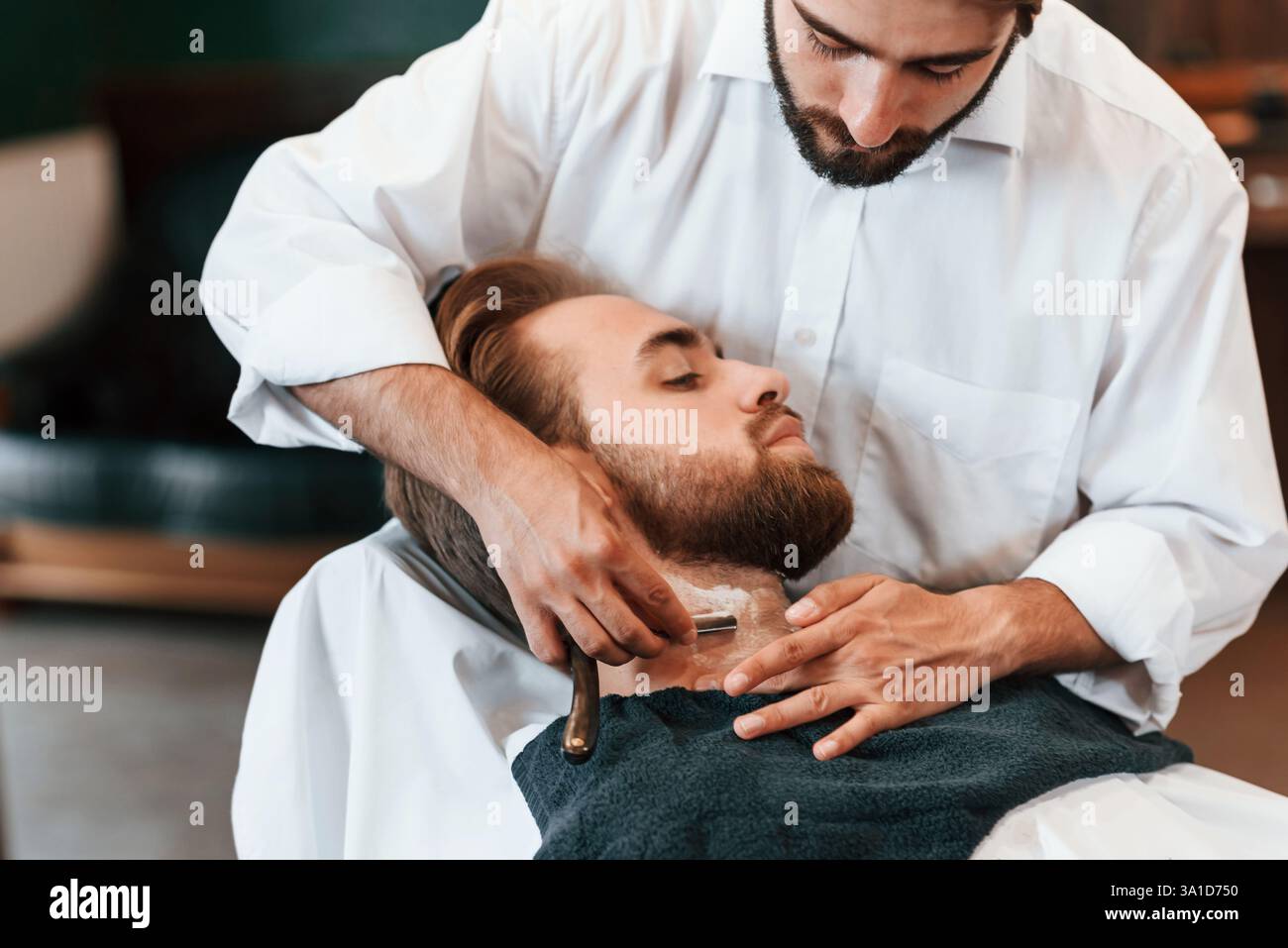 On the neck, shaving the beard. Man is visiting modern barber shop ...