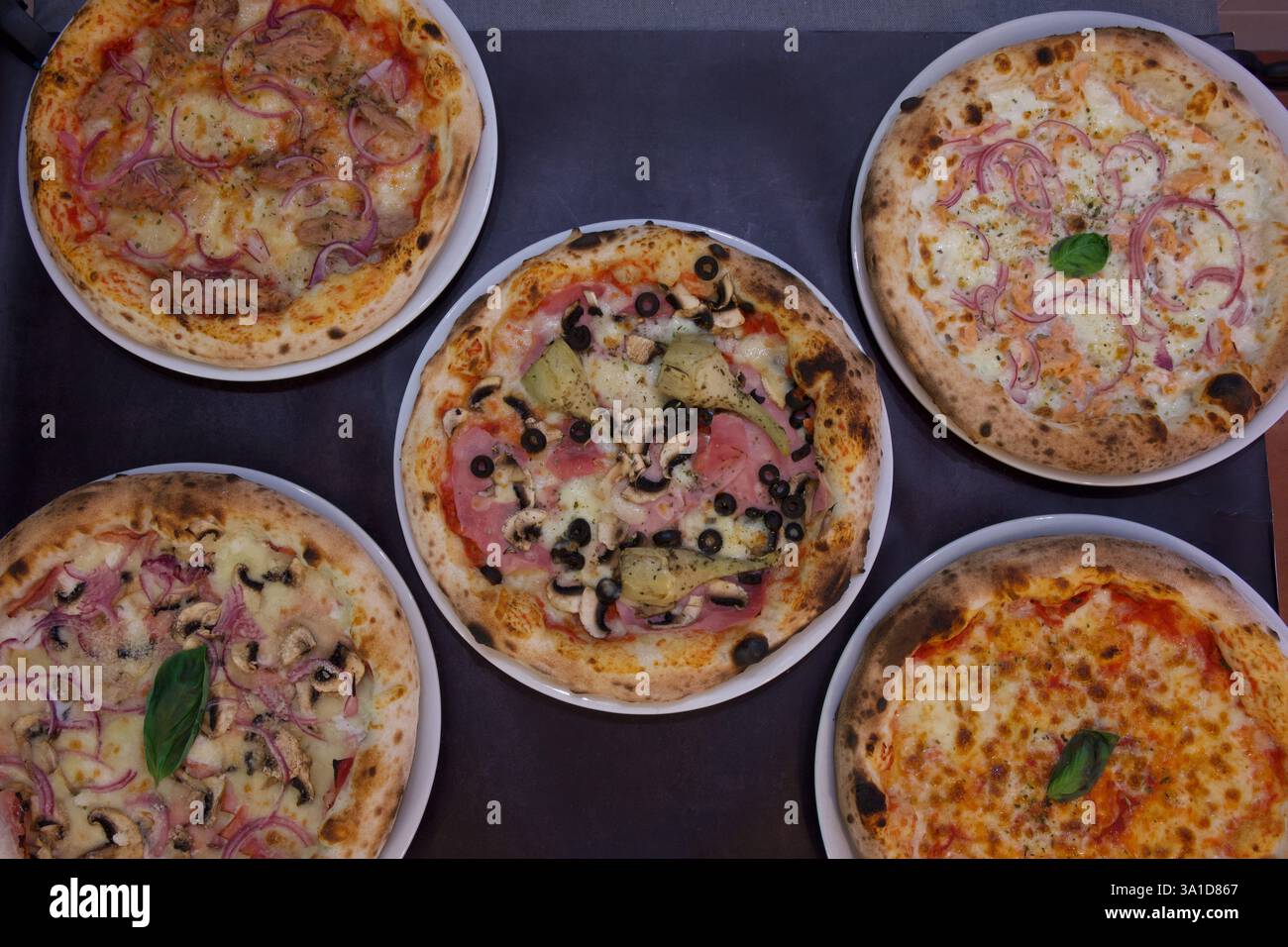 Five different pizzas with various toppings are displayed on a black ...