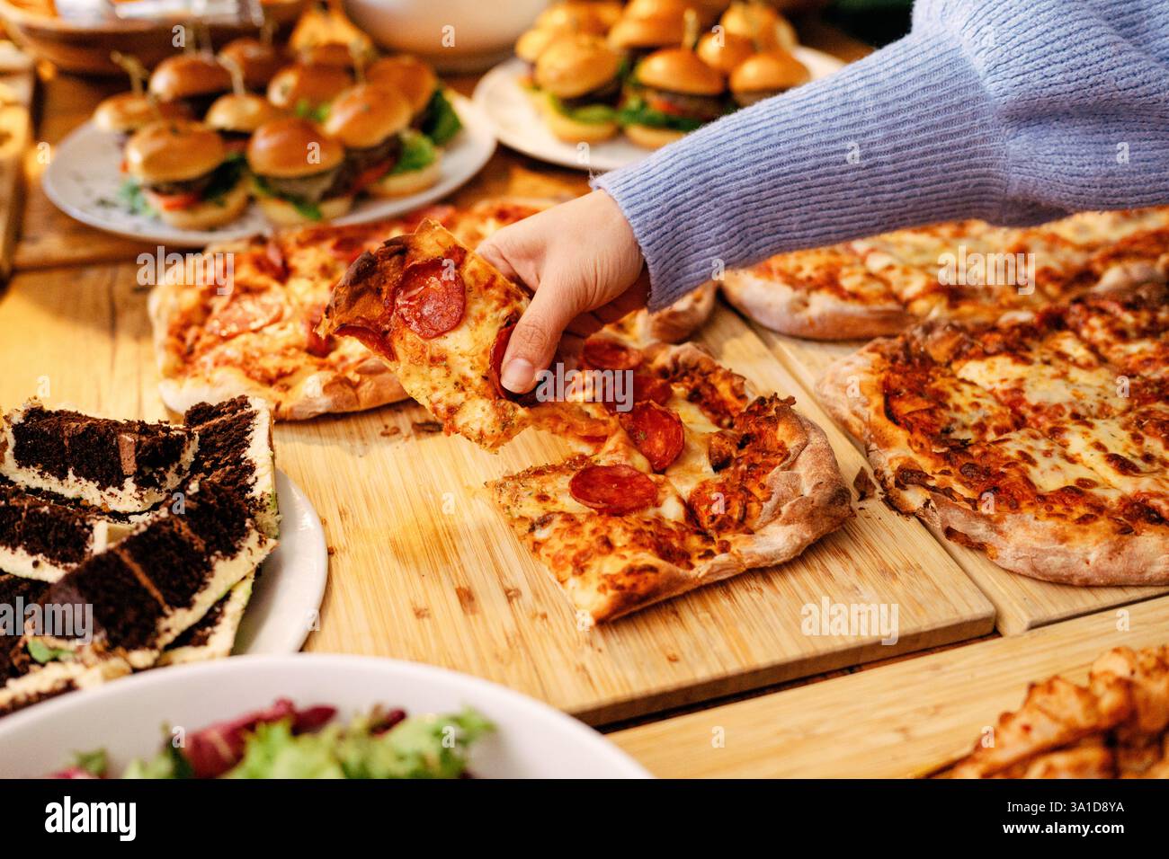 Hand Grabbing Pizza Slice With Assorted Snacks on Wooden Dining Table ...