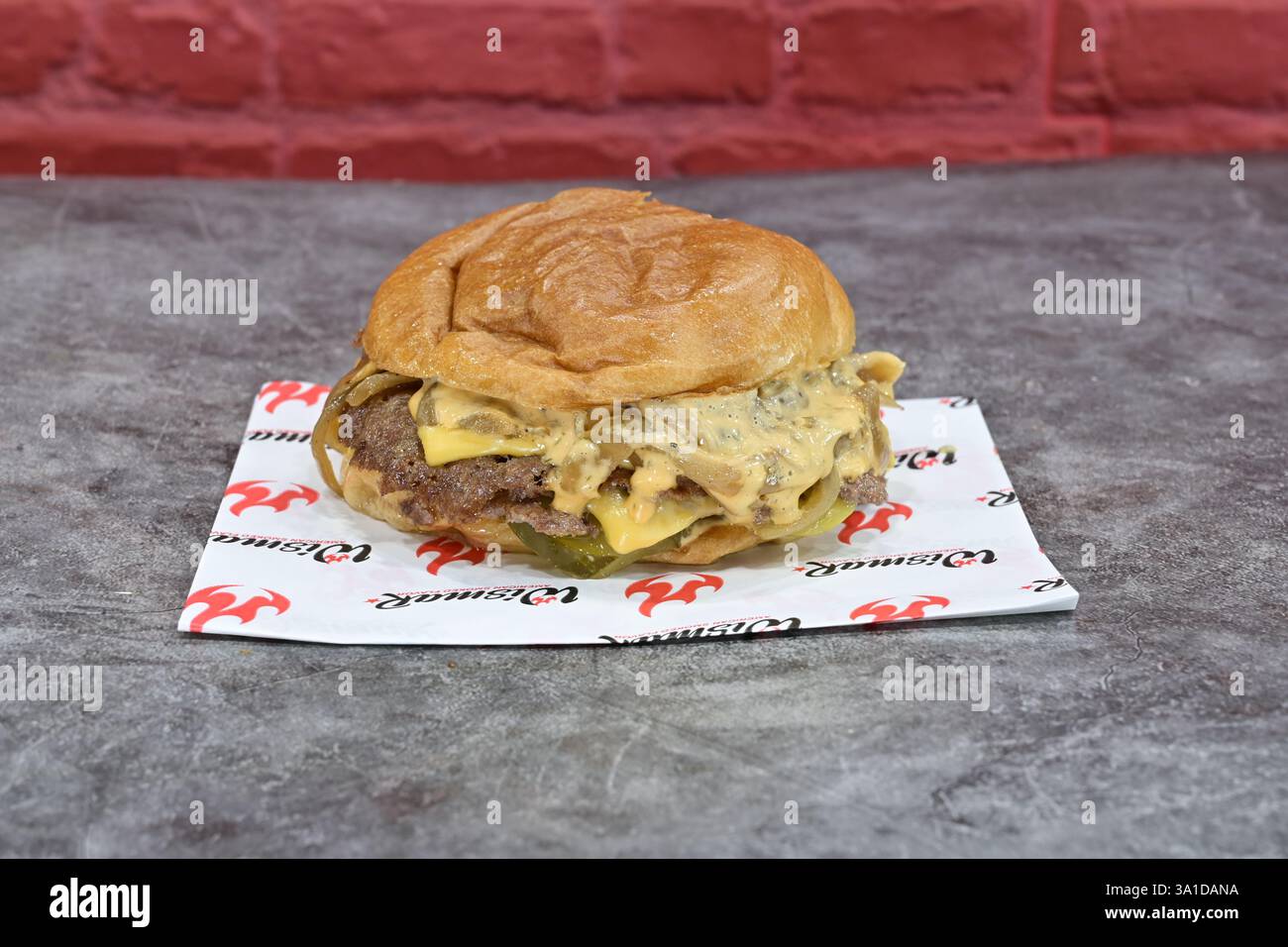 A burger with cheese and onions on a bun sits on a red and white napkin ...