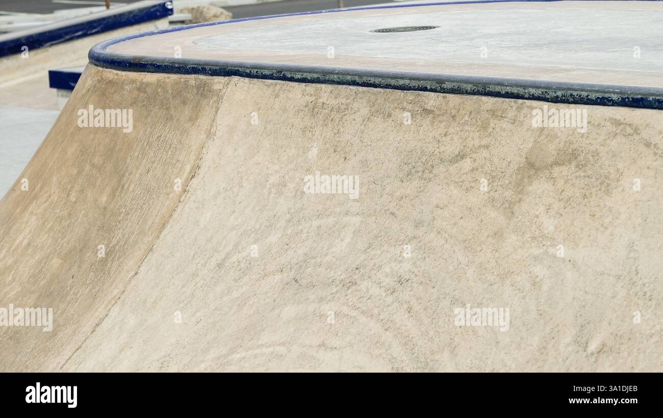In an urban skate park, a concrete ramp with vibrant blue edges creates ...