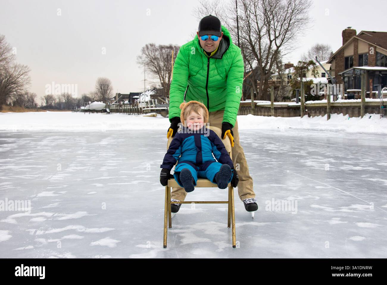 Father skating on a frozen pond while pushing his toddler son in a ...