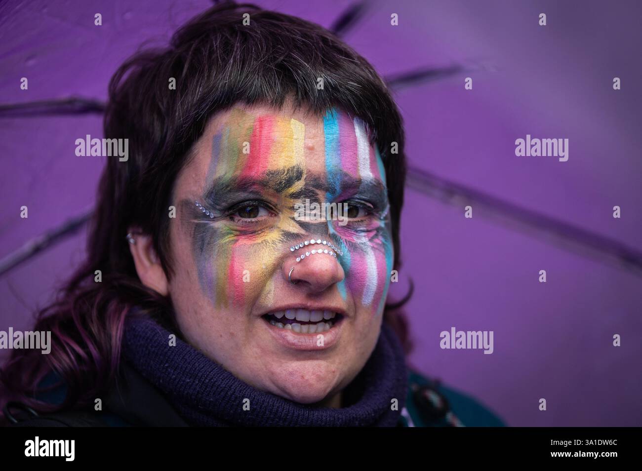 A woman with her face painted with the Rainbow and trans flags is seen ...