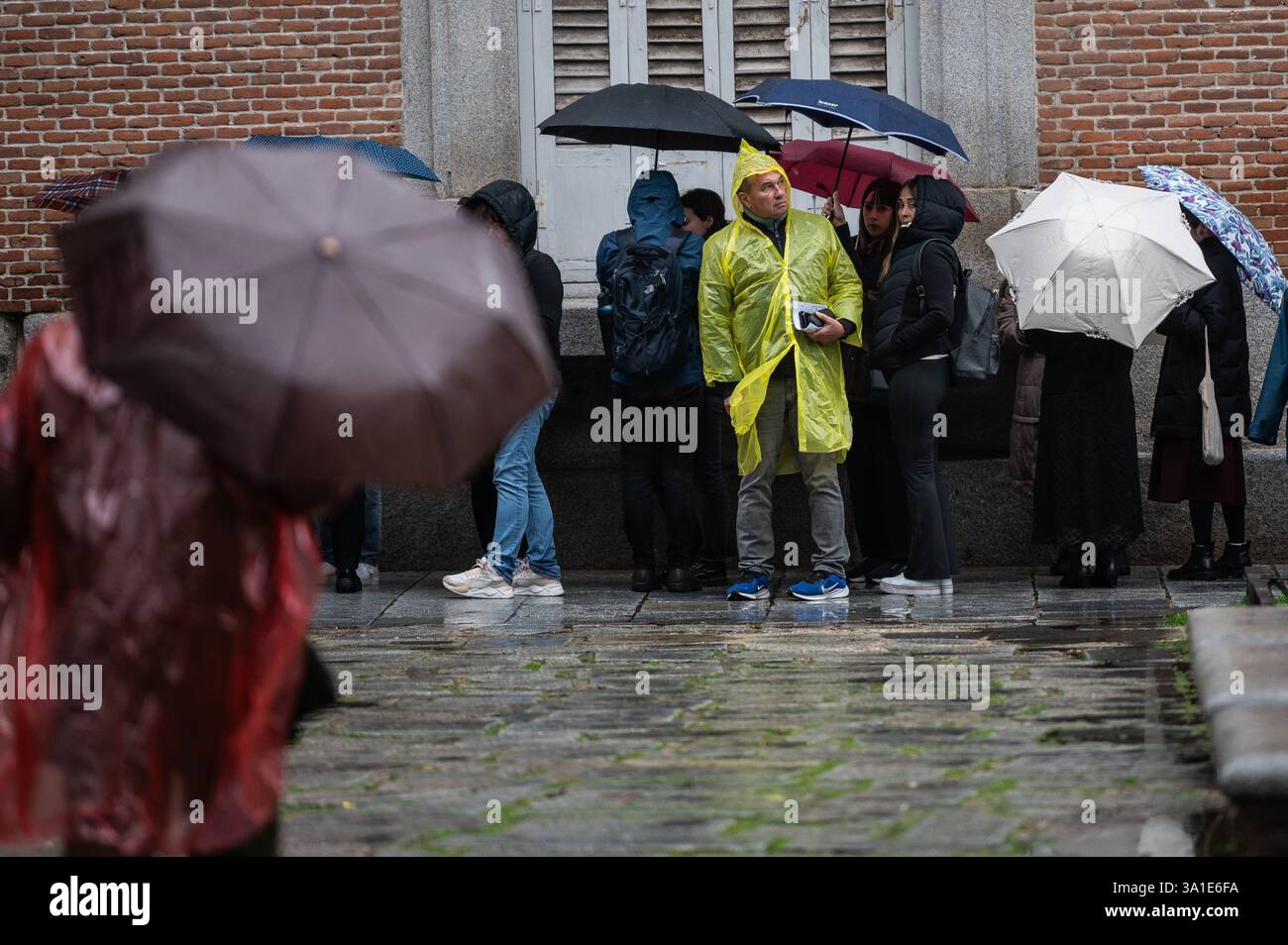 People with umbrellas and raincoats queue under the rain waiting to ...