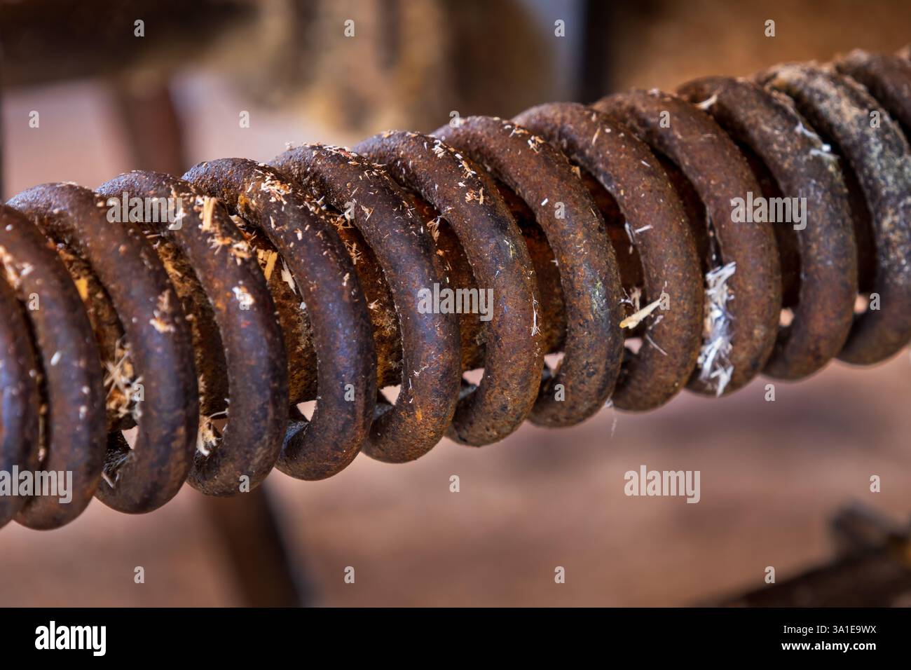 Close-up of a rusted spring coiled around a bar, covered in sawdust ...