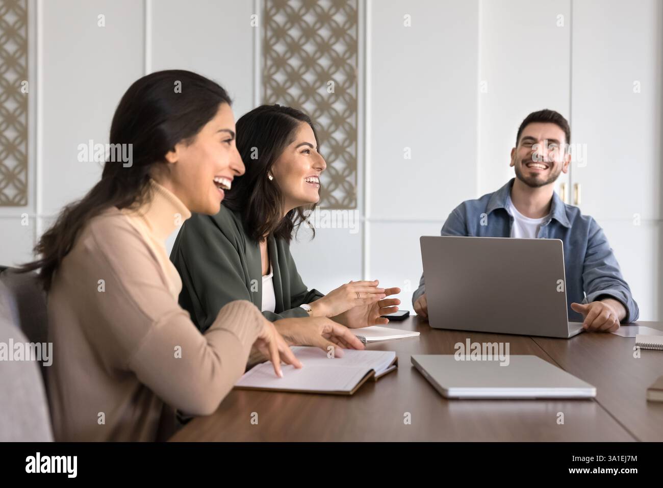 Diverse employees sit at conference table engaged in positive ...