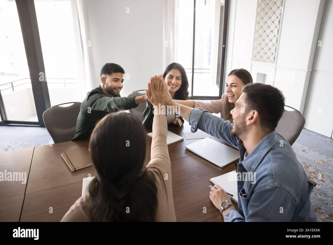 Five colleagues giving high-five gesture seated around conference table ...